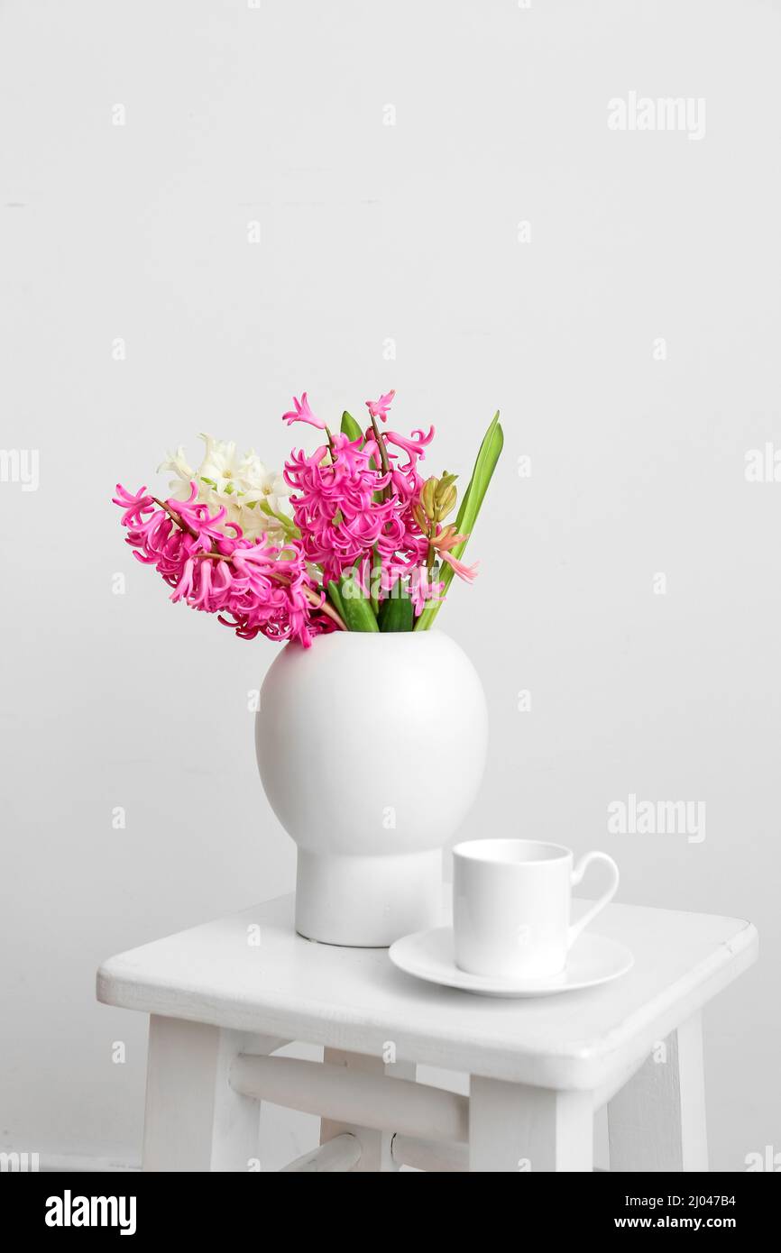 Vase with hyacinth flowers and cup on stool near white wall Stock Photo ...