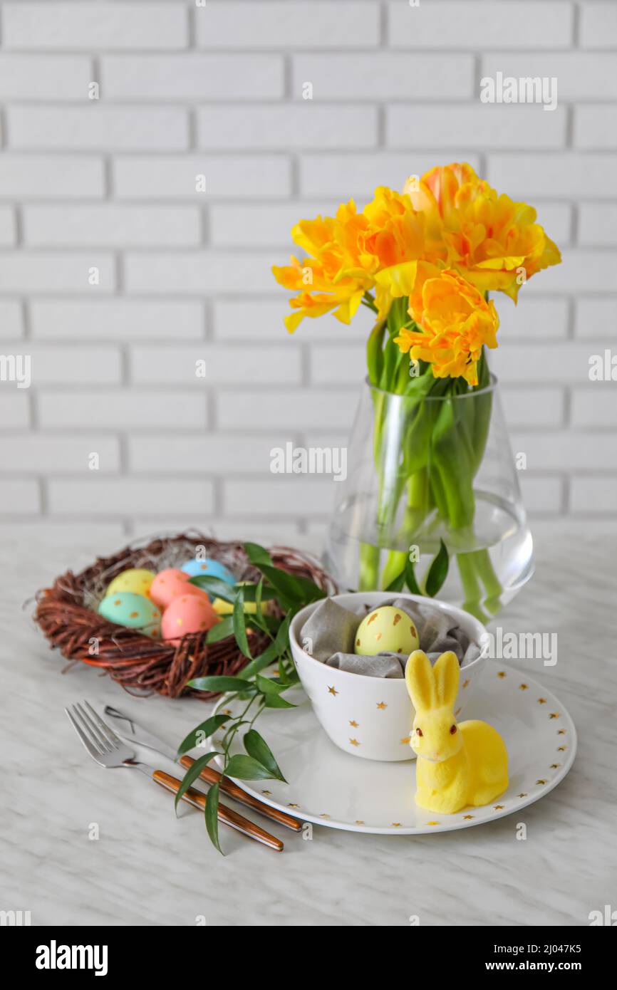 Beautiful setting, Easter eggs and vase with tulips on table near white ...