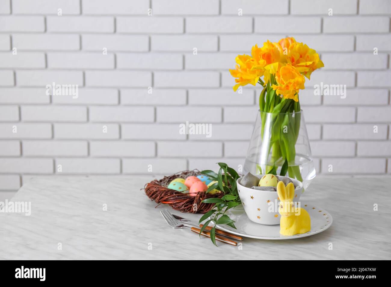 Beautiful setting, Easter eggs and vase with tulips on table near white ...
