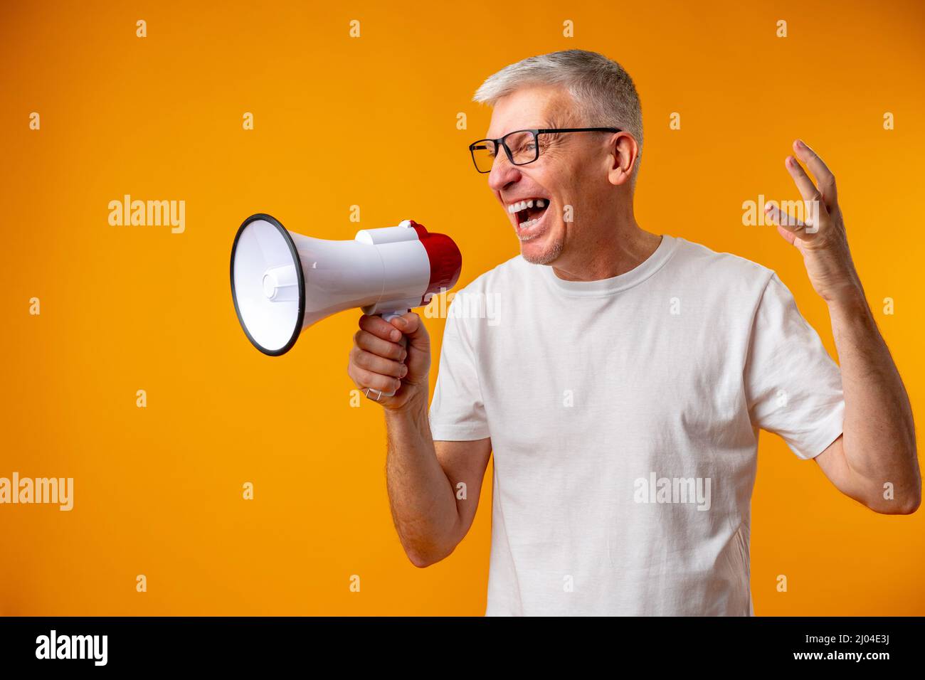 Portrait of mature man shouting with megaphone against yellow ...