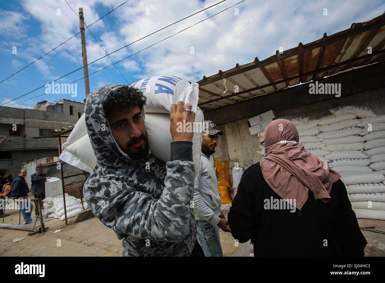 A Palestinian vendor carries bags of flour on the shoulder in front of ...