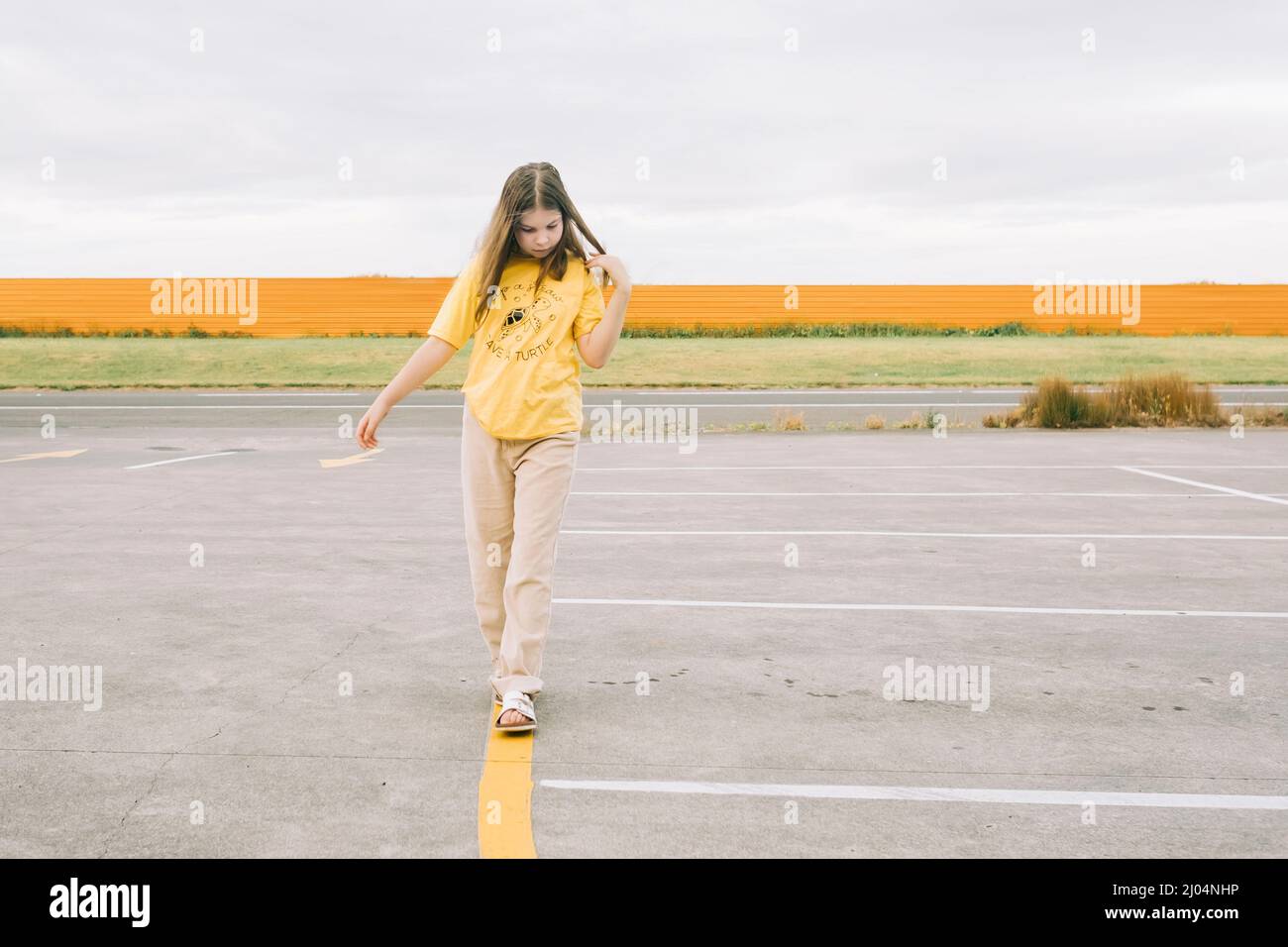 Young girl walking along painted yellow line in car park Stock Photo ...