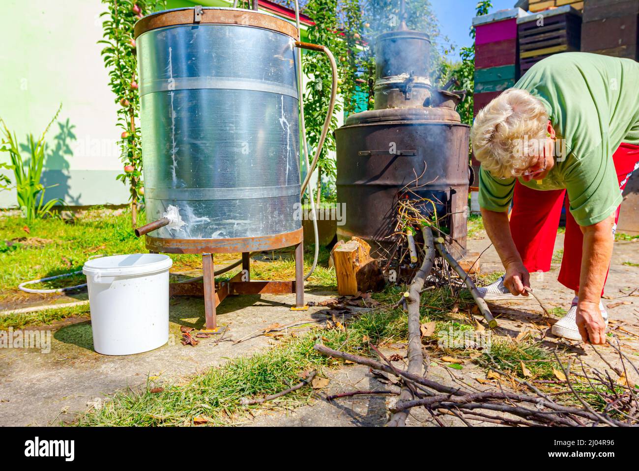 Grandma throws dry branches into the firebox of a homemade distillery ...