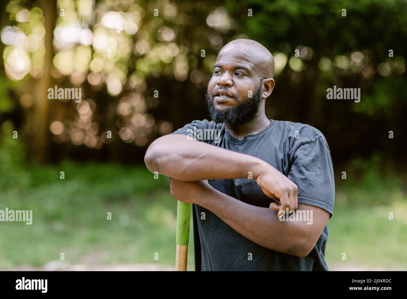 Black farmer with a contemplative look leans on a farm tool Stock Photo ...