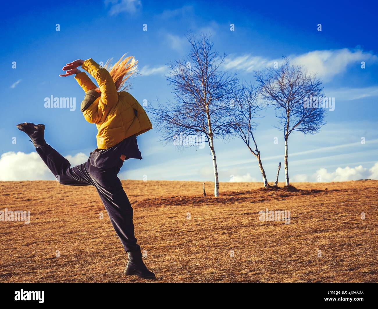 Woman jumping throwing her leg back on an autumn field against a blue ...
