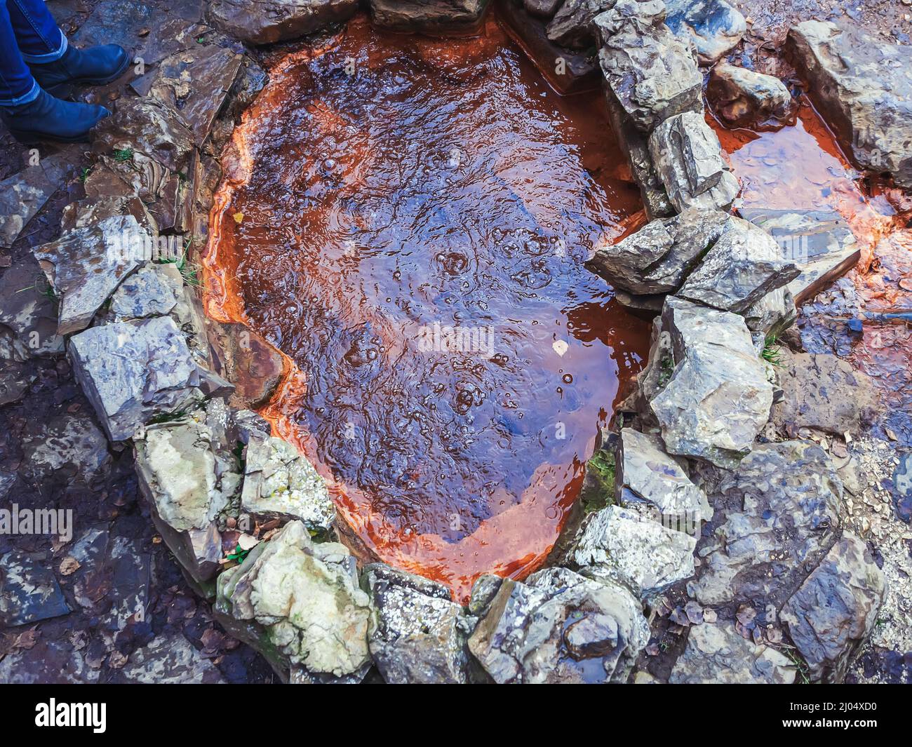 Outdoors, a shallow, rusty stone well with bubbling mineral water ...