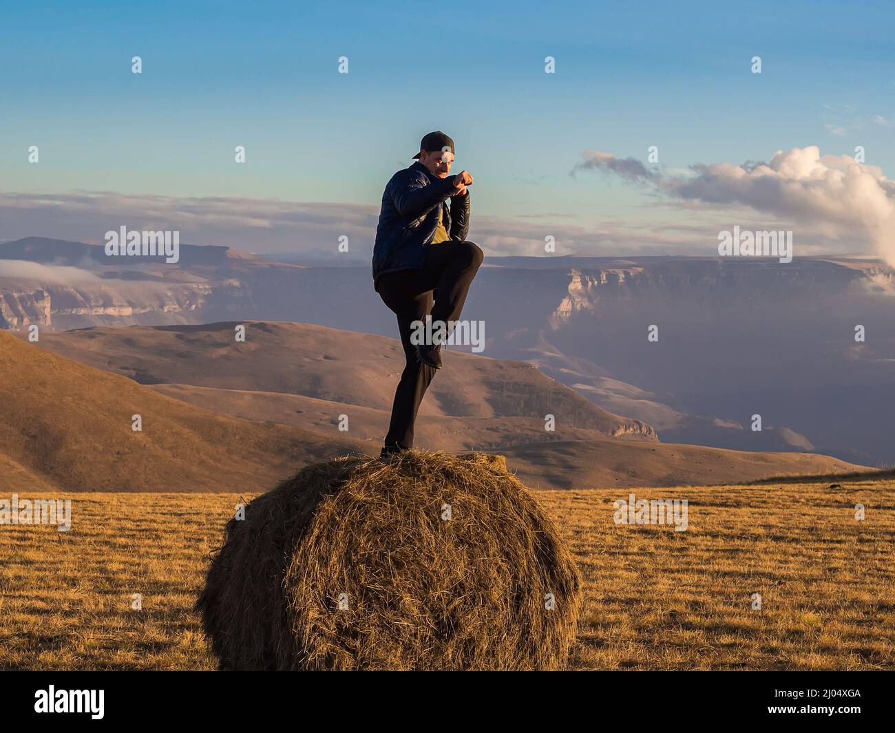 A man stands in fighting pose on one leg on a haystack in an autumn ...