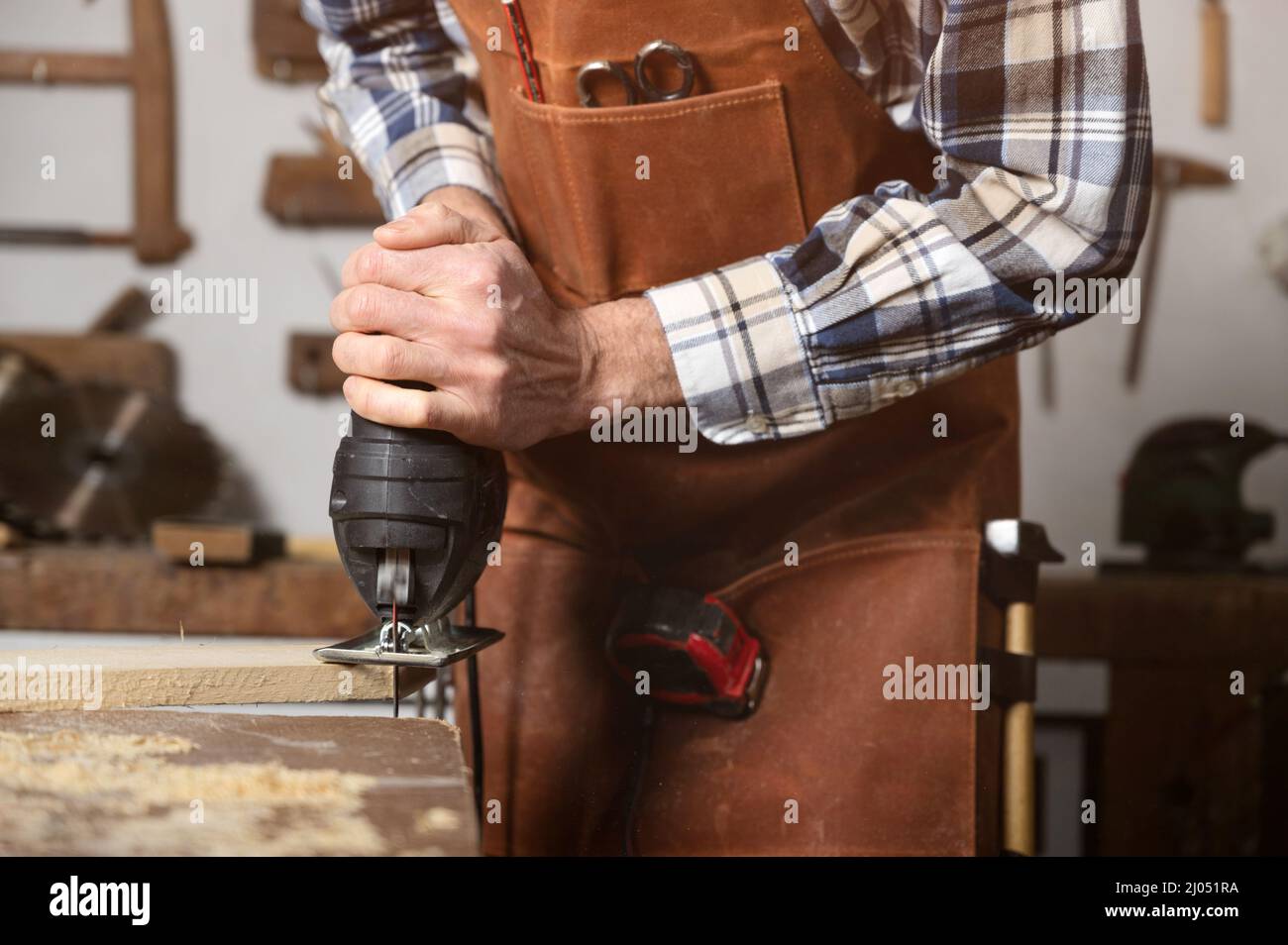 Carpenter is sawing a wood plank with electric jig saw machine in ...