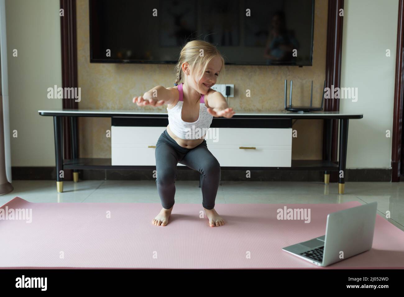 Cute little girl in sportswear doing fitness exercises at home. Distant ...