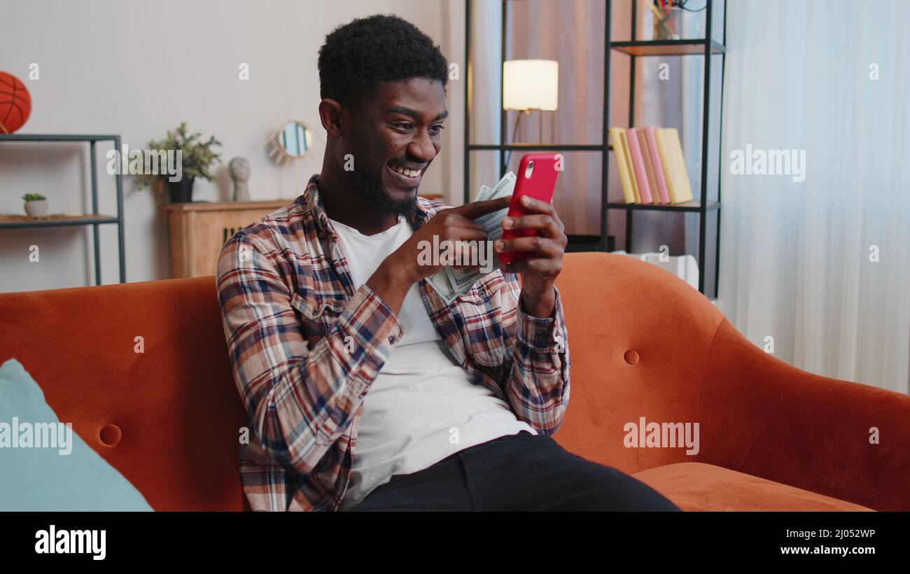Smiling happy young man counting money cash and use mobile phone ...