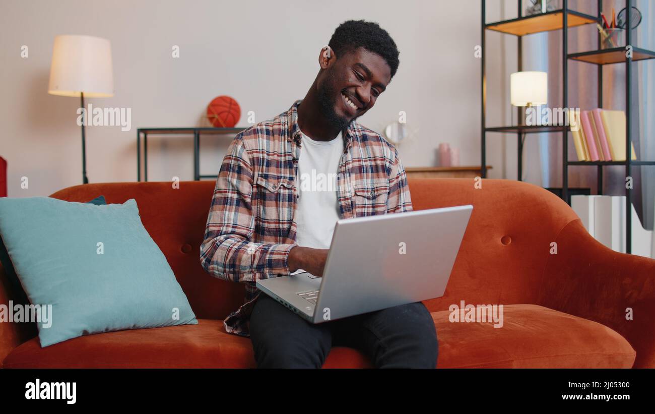 African American young man sitting on sofa closing laptop pc after work ...