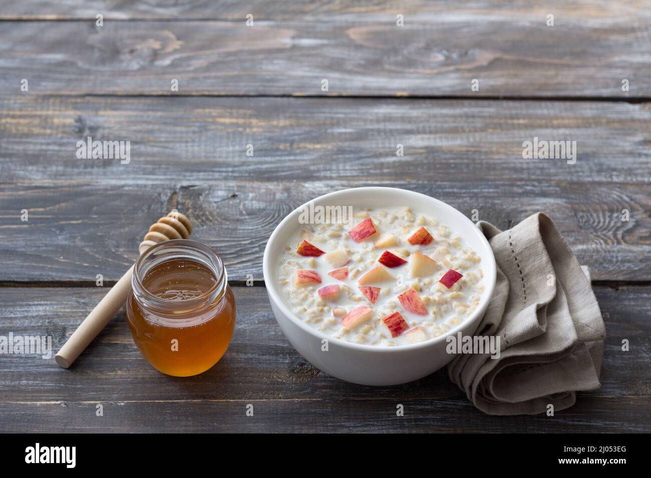 Milk oatmeal porridge with apple and honey in white bowl on wooden ...