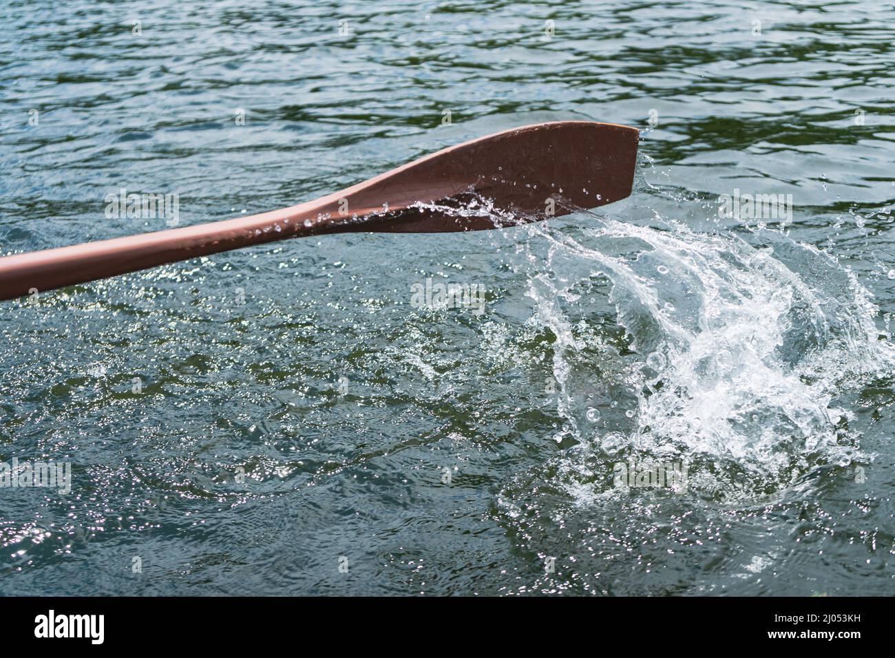 Wooden rowing oar touching water causing splash and ripples in the sea ...