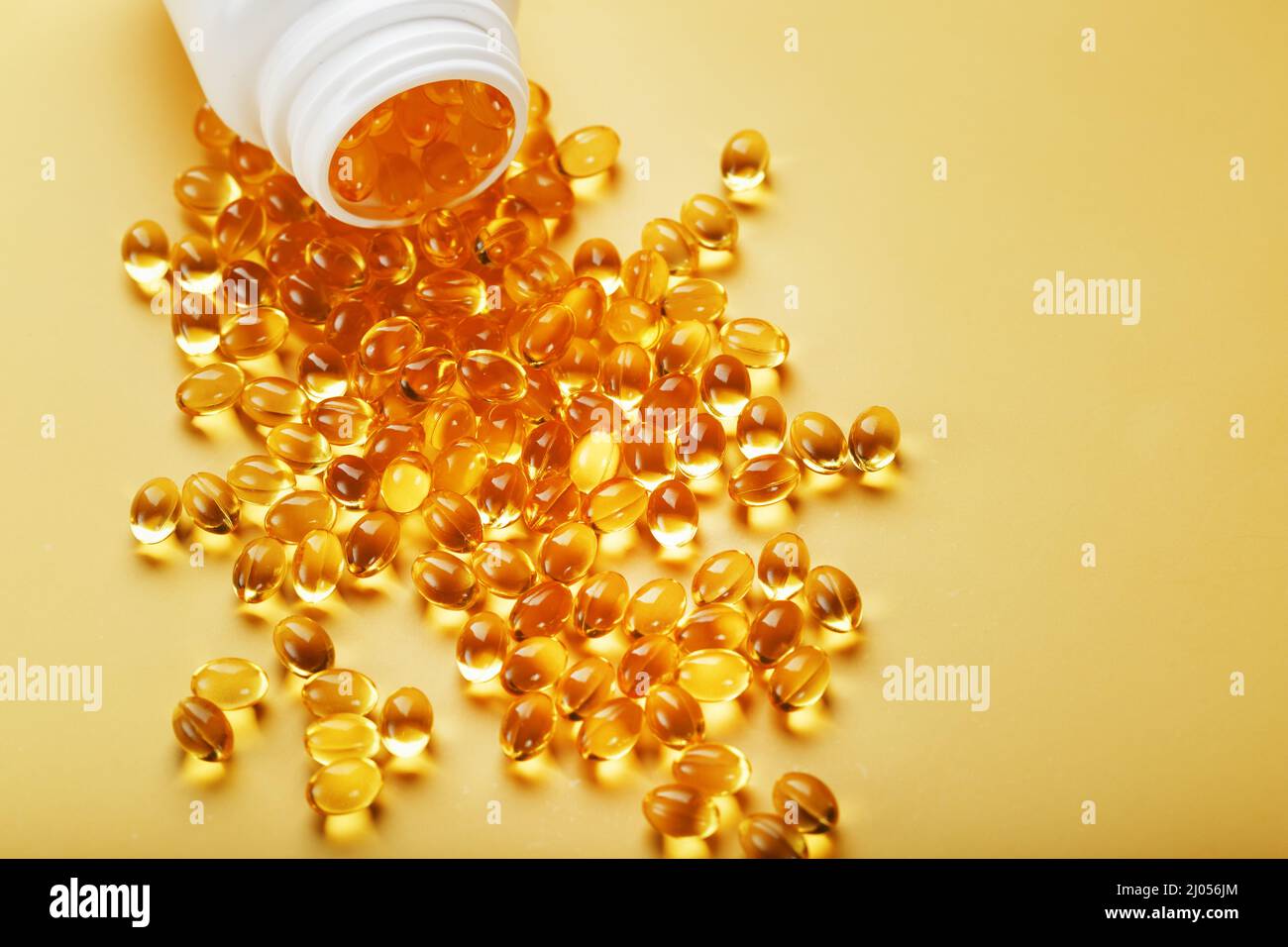 Gold Vitamin D3 capsules poured out of a jar on a yellow background ...