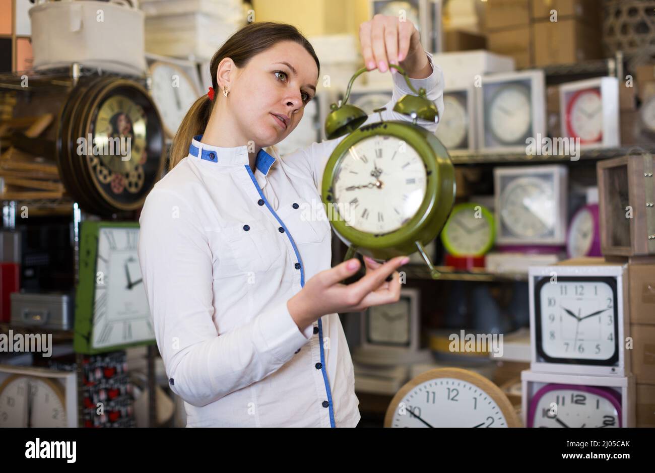 Positive woman is standing with modern clock in furniture store Stock ...
