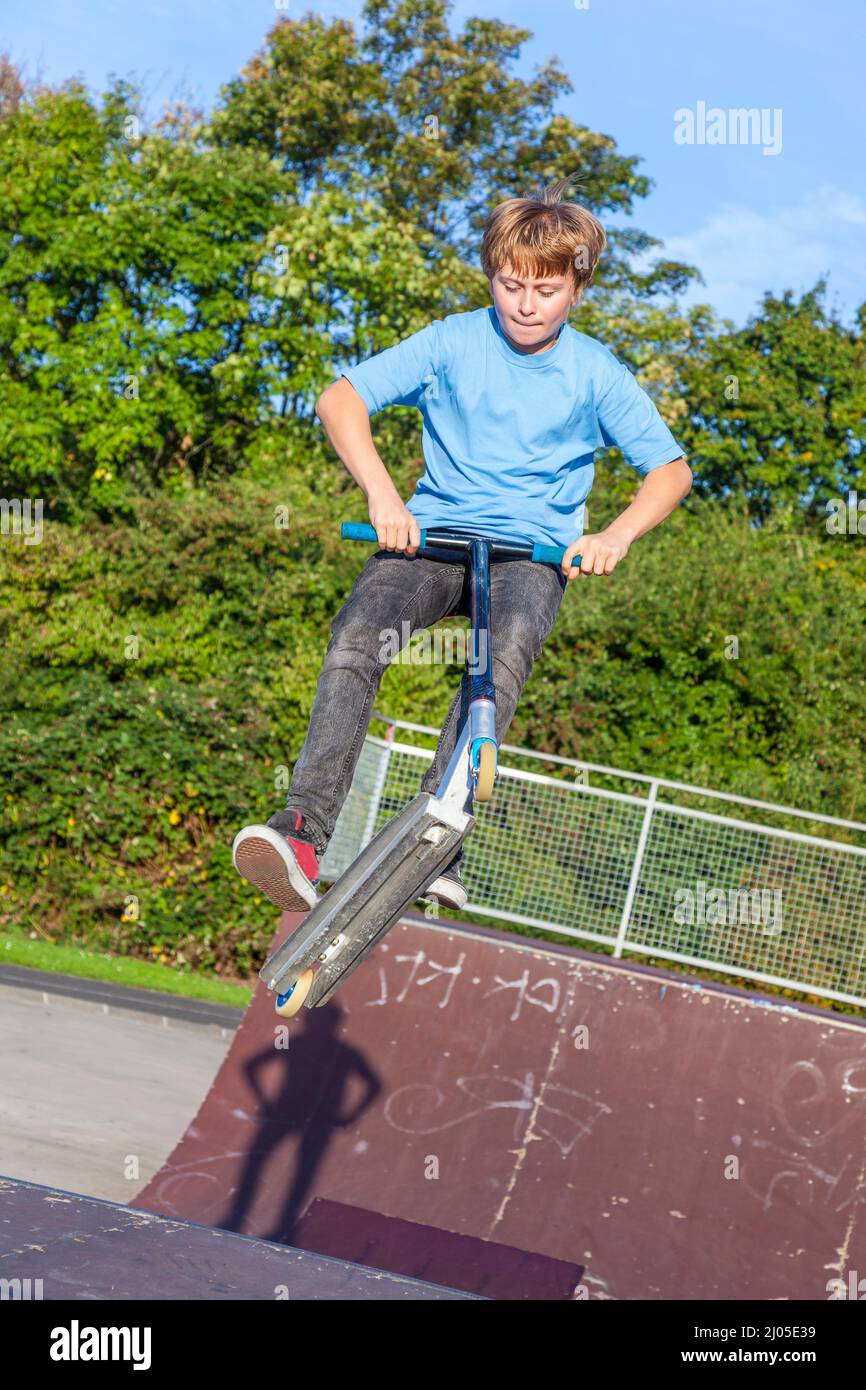 boy jumps with scooter at the skate park over a ramp and has fun Stock ...
