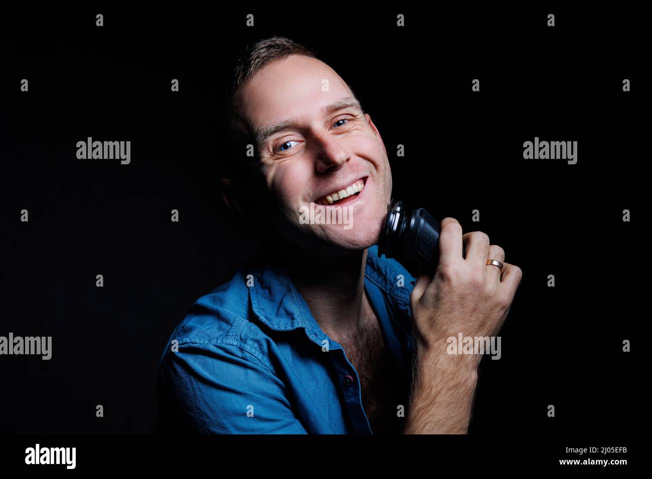 A young handsome man shaves his stubble with a modern electronic razor ...