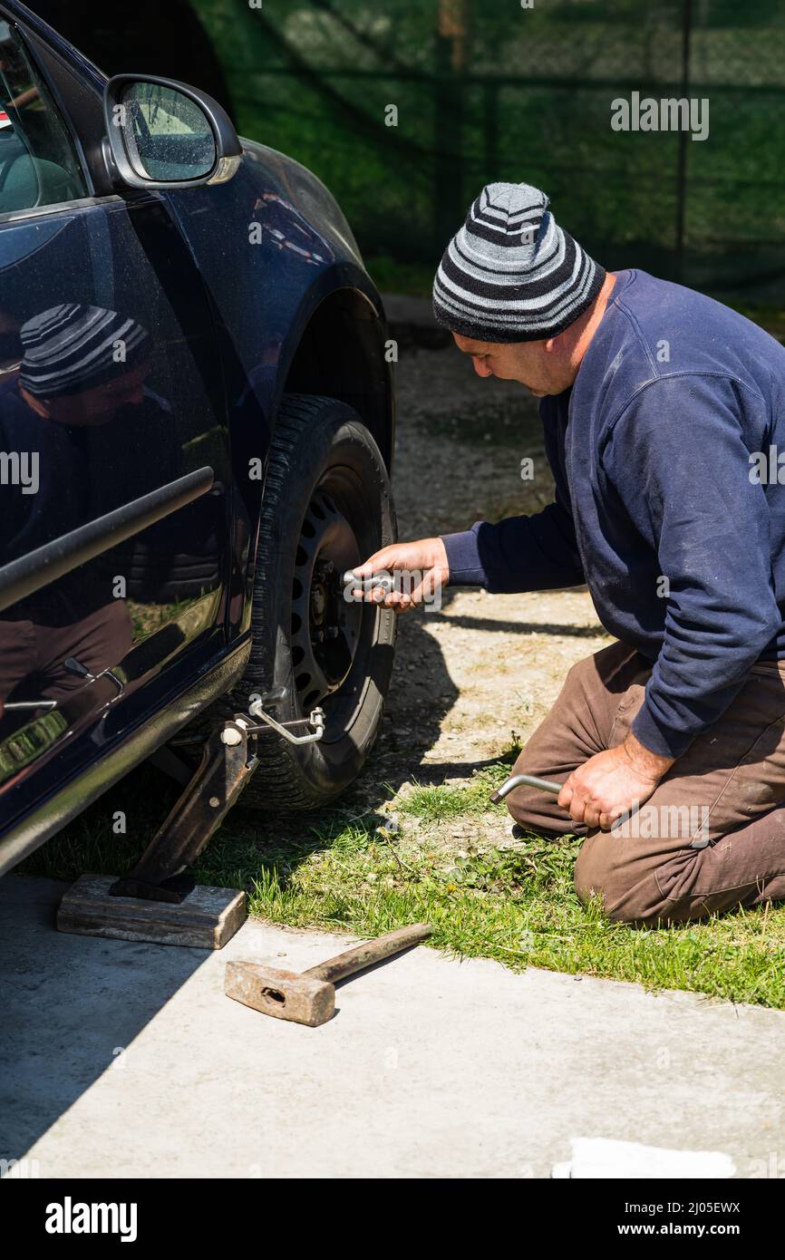 Mechanic changing wheel on car with manual wrench. Mechanic replacing ...