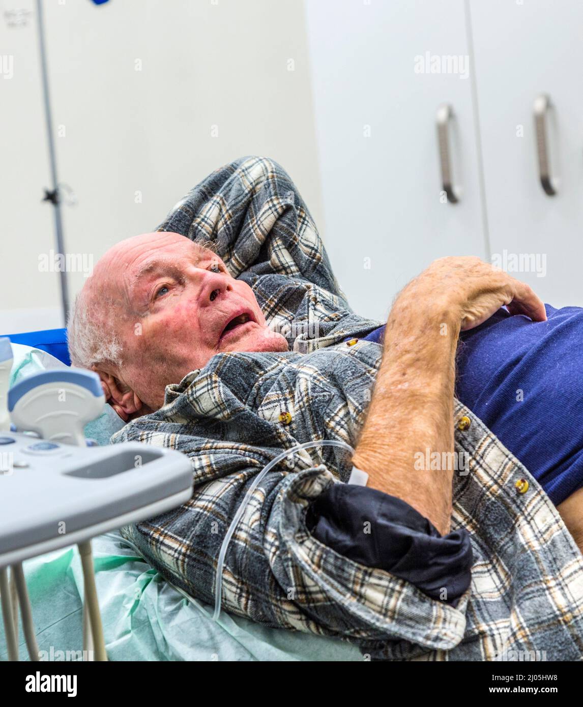 Sick senior lying in a hospital bed with iv drip attached on his hand ...