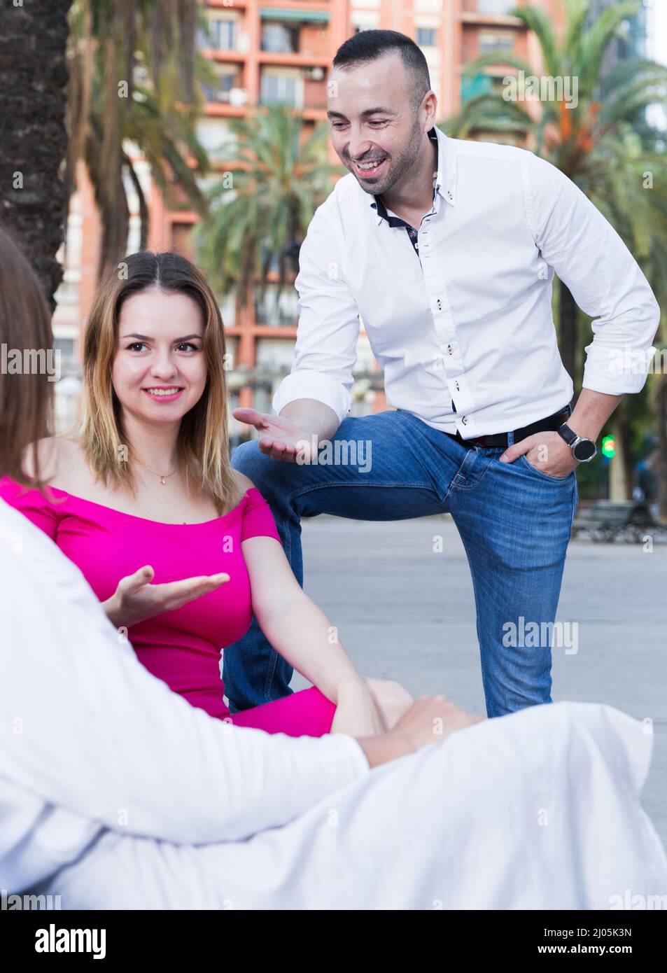 Guy is talking with smiling stranger women who are sitting on the bench ...