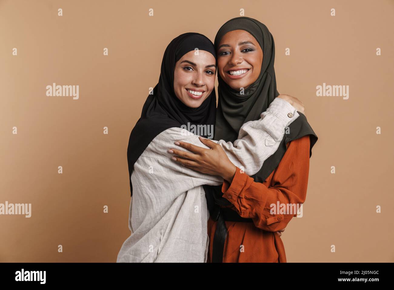 Young muslim women in hijab hugging and smiling at camera isolated over ...