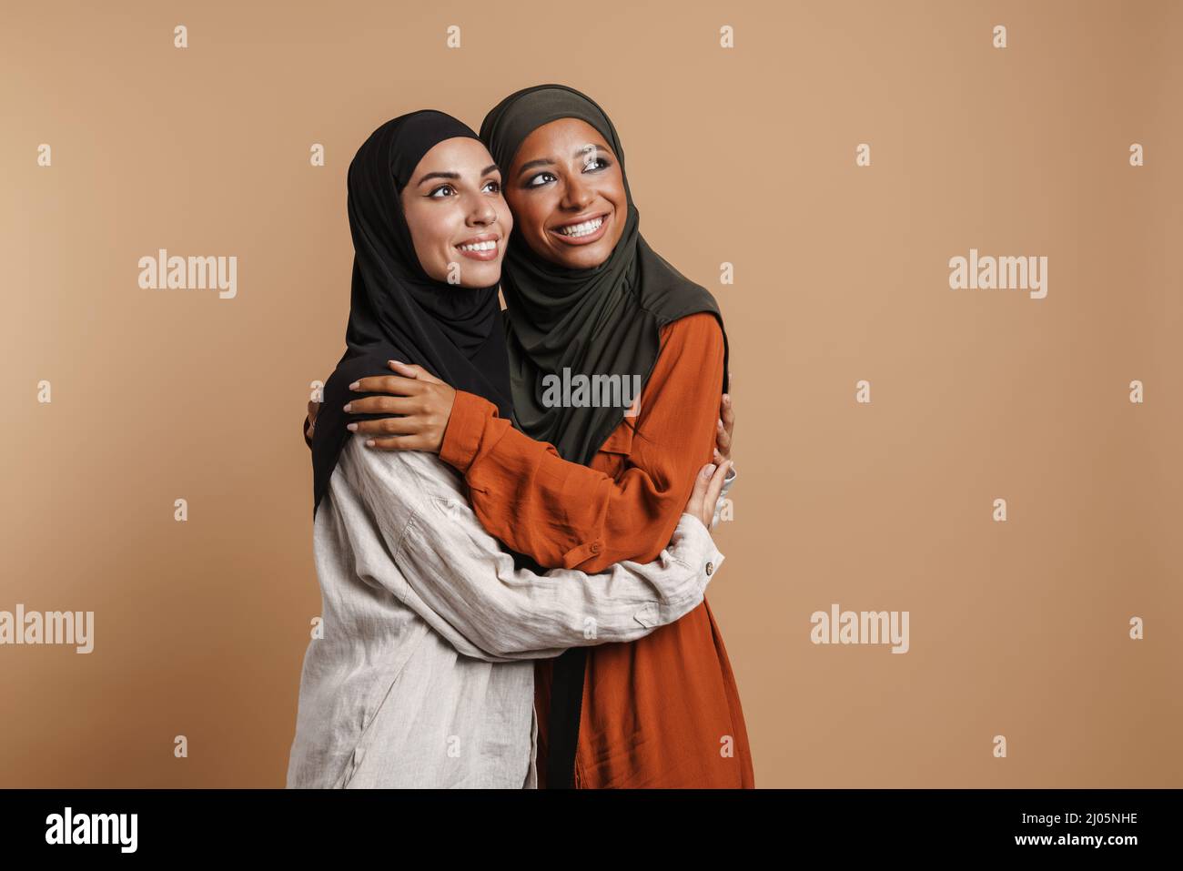 Young muslim women in hijab hugging and smiling at camera isolated over ...