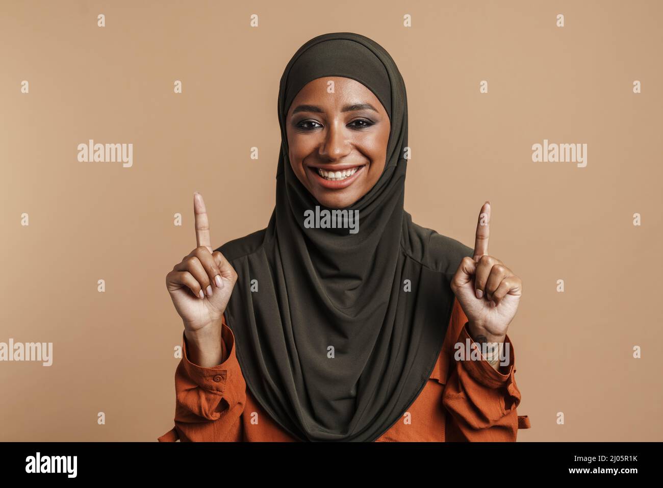 Young muslim woman in hijab smiling and pointing fingers upward ...