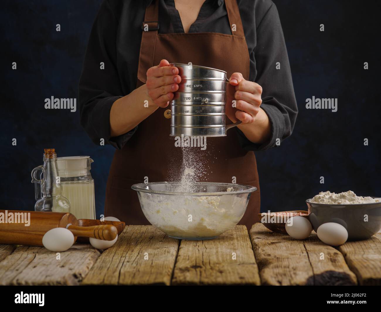 Chef prepares dough at table, dark background. Sifts flour through a ...