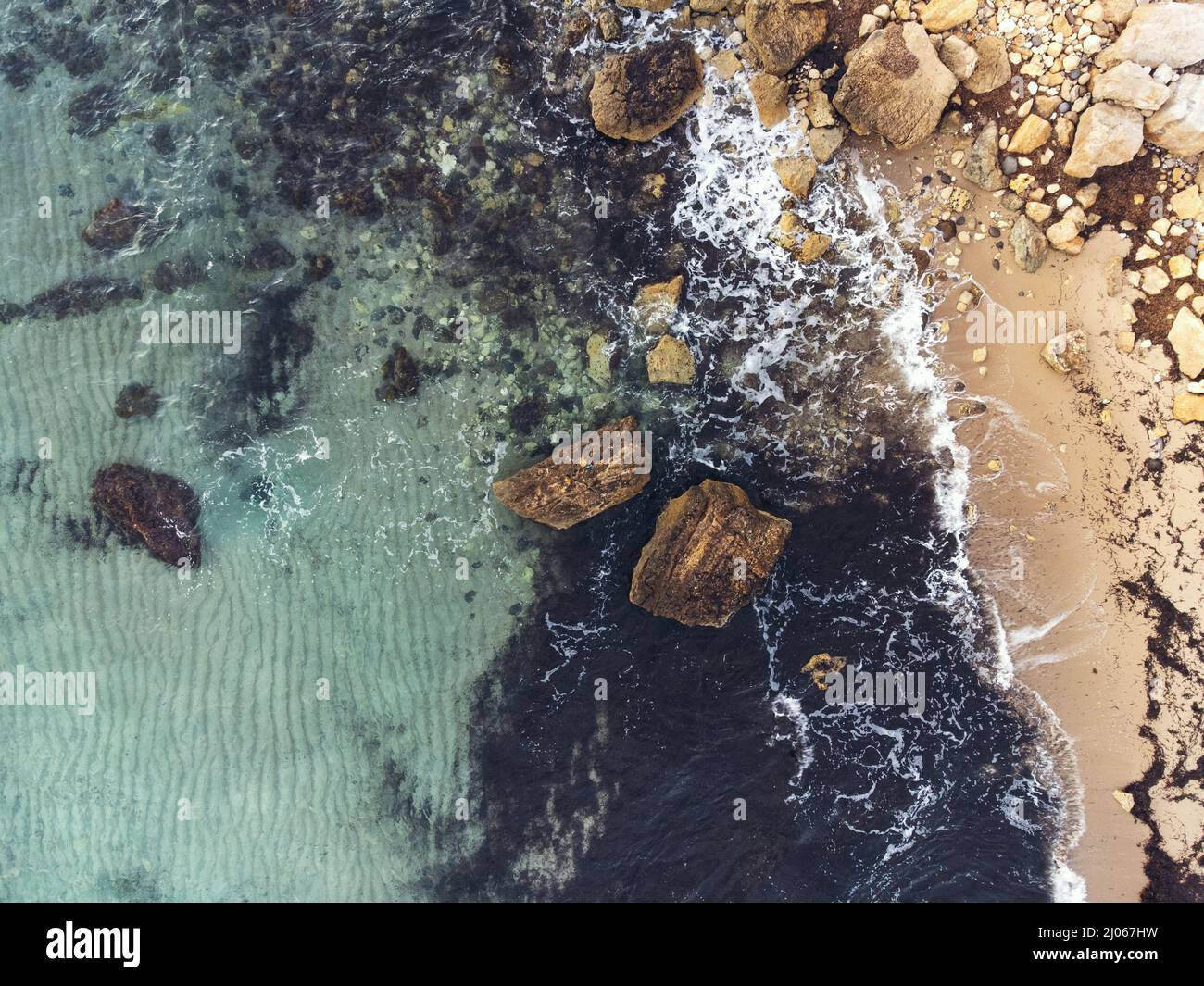 Aerial top view of a rocky beach with a blue colored sea and yellow ...