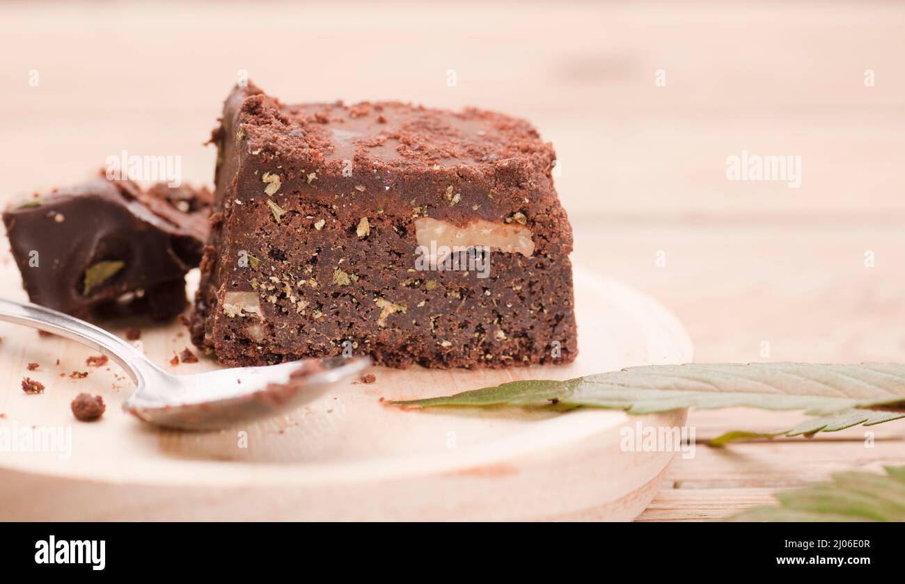 piece of brownie with marijuana, on wooden board with spoon and green ...