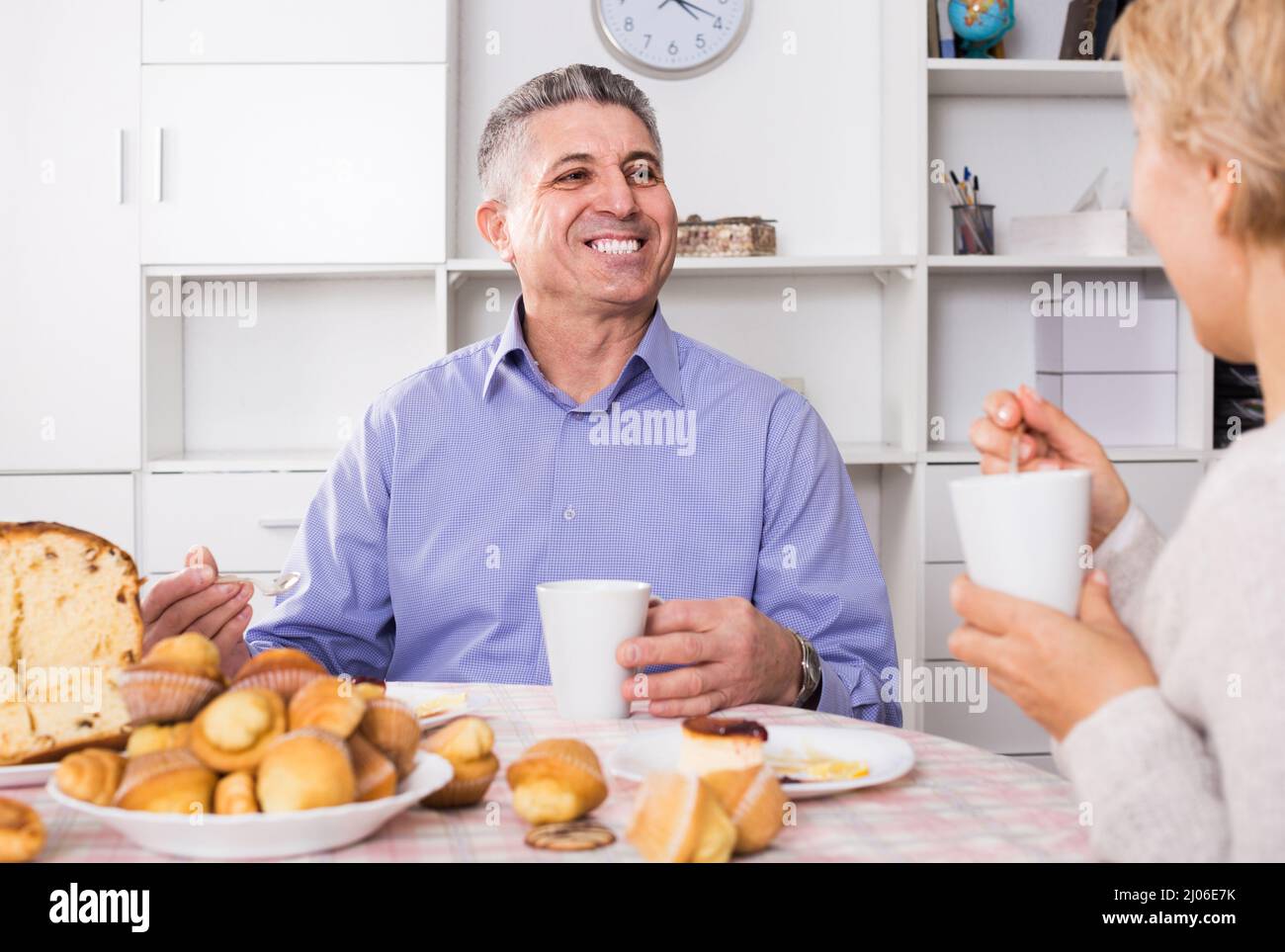 Wife treats smiling italian husband with tasty pastries at table at ...