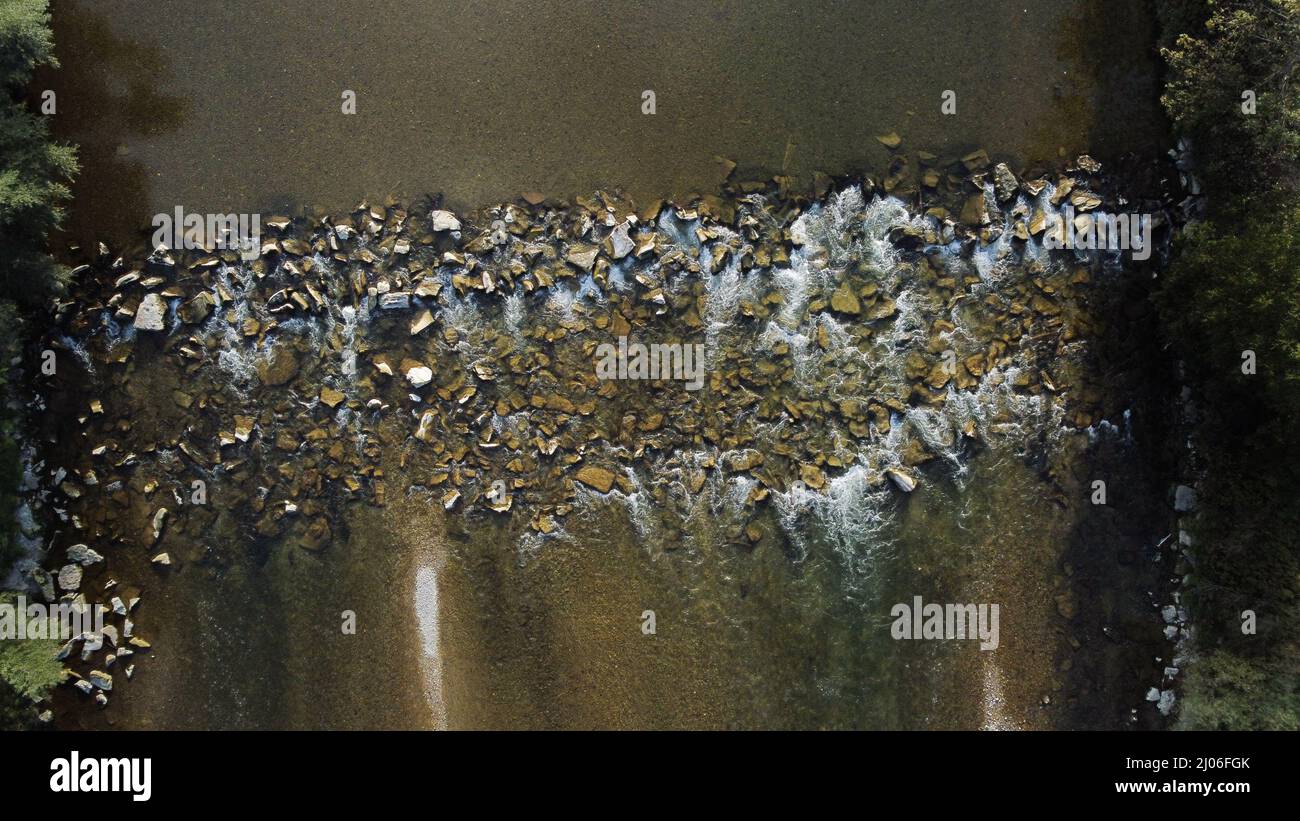 Aerial view of a a little dam of rocks in a flowing river in the forest ...