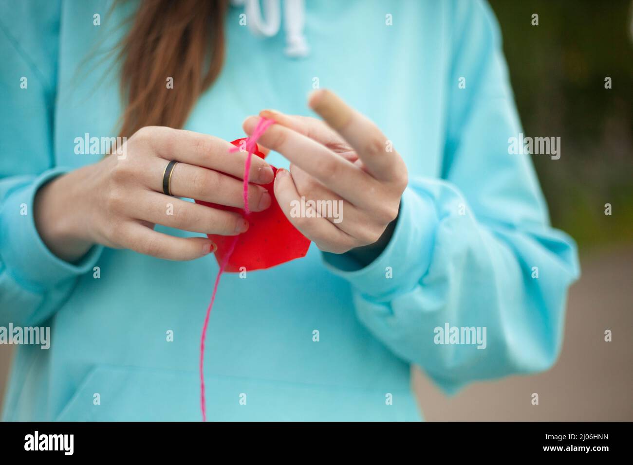 Child ties thread to heart. Girl holds red cardboard in her hands ...