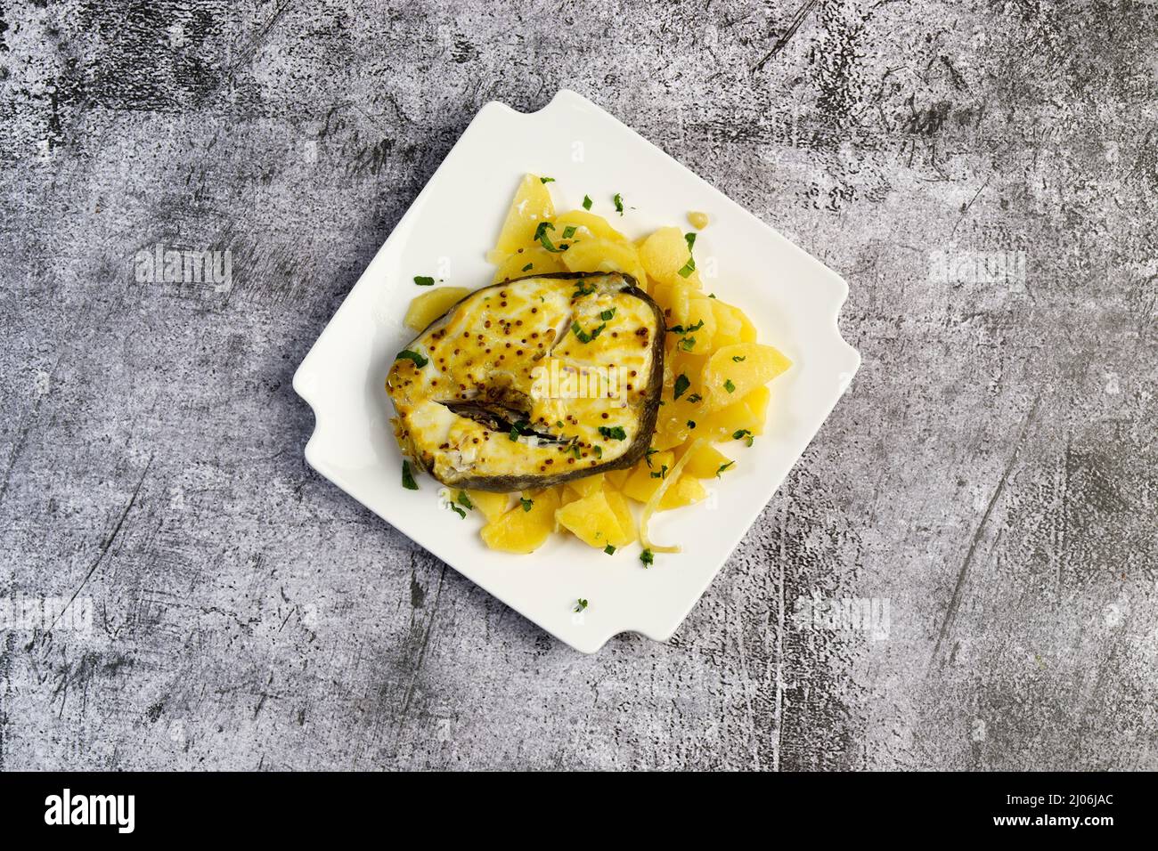 Oven baked cod with potatoes on a white square plate on a dark ...