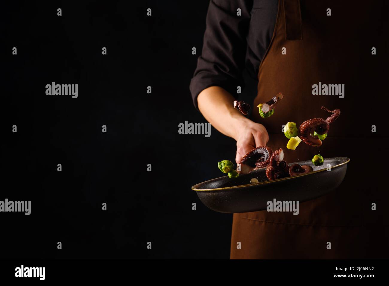 A professional chef in a dark uniform cooks octopus with vegetables in ...