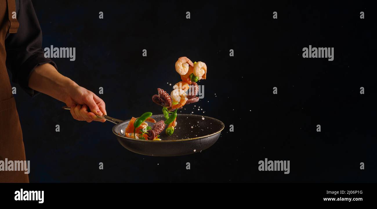 On a dark background, a frying pan in the chef's hand with seafood ...