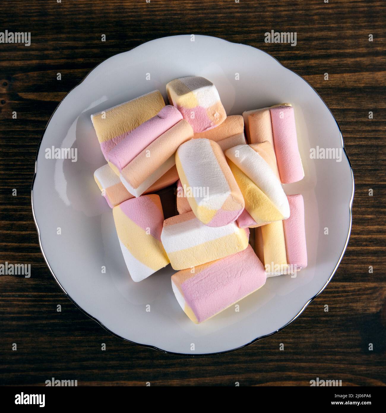 Stack of colorful marshmallows on a white plate on a wooden texture ...