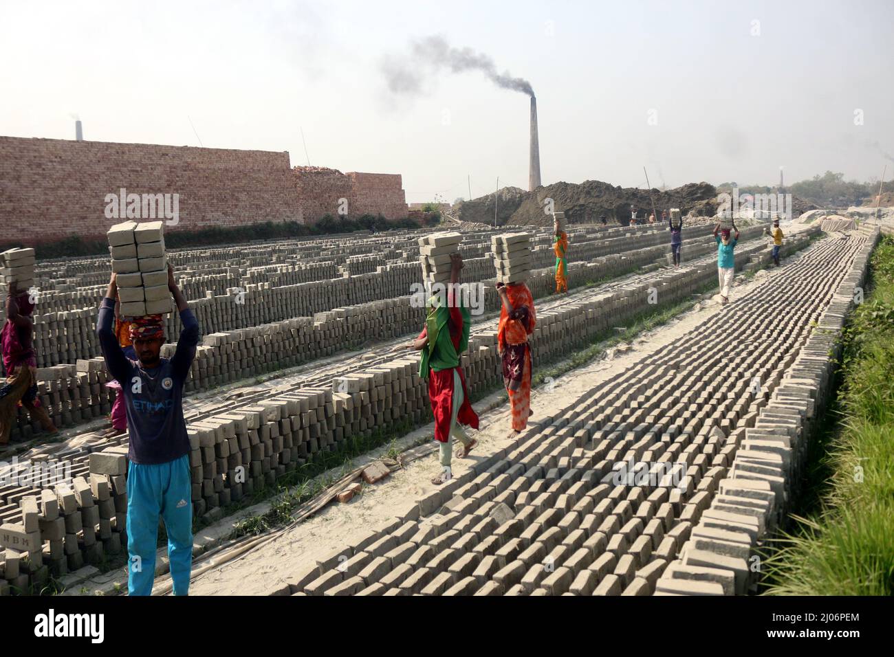 Workers transport bricks on their heads at a brick factory. Due to the ...