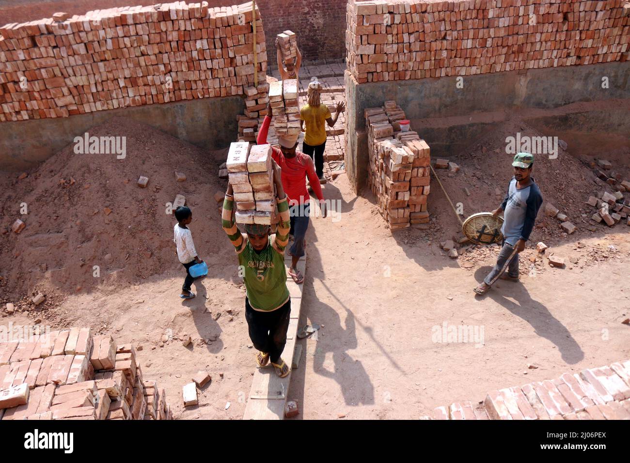 Workers transport bricks on their heads at a brick factory. Due to the ...