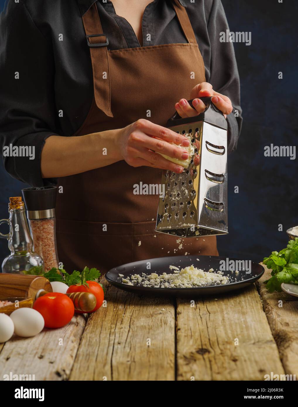 A professional chef in a dark uniform grates cheese. Vegetables, eggs ...