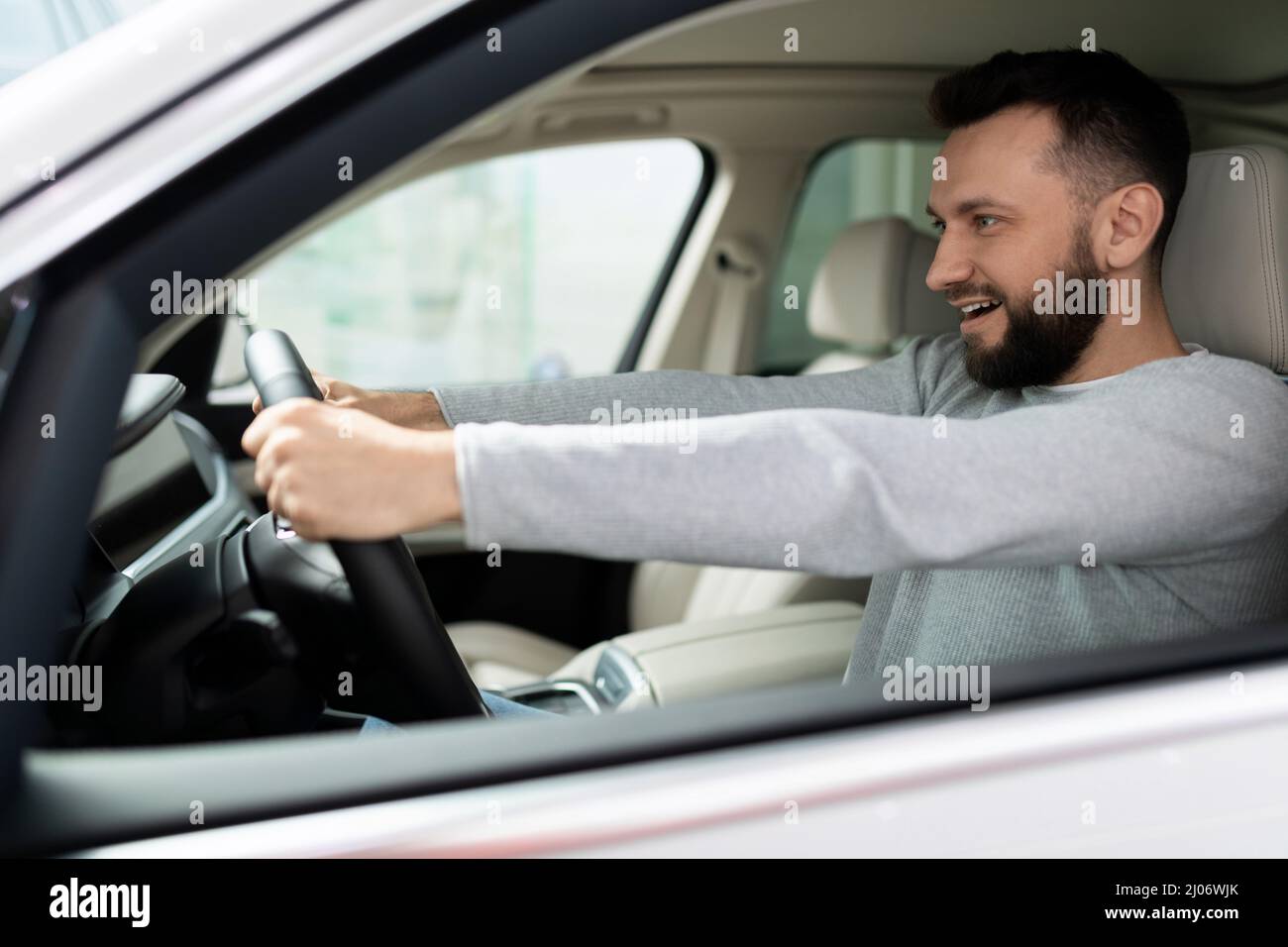 novice driver behind the wheel of a new car looks ahead with a smile ...