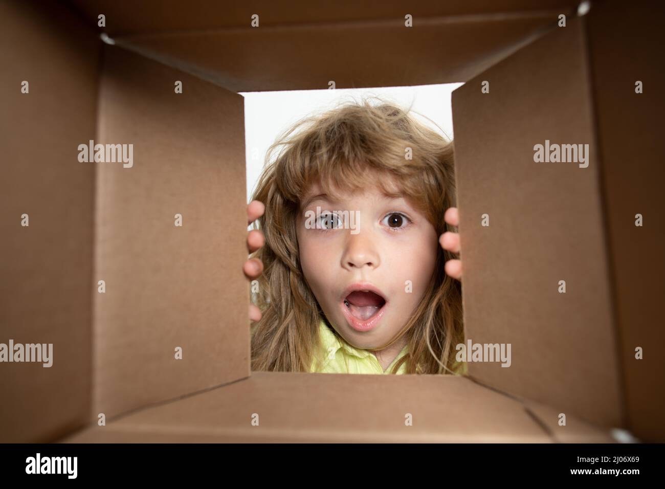 Happy little child boy is opening gift and looking inside cardboard box ...
