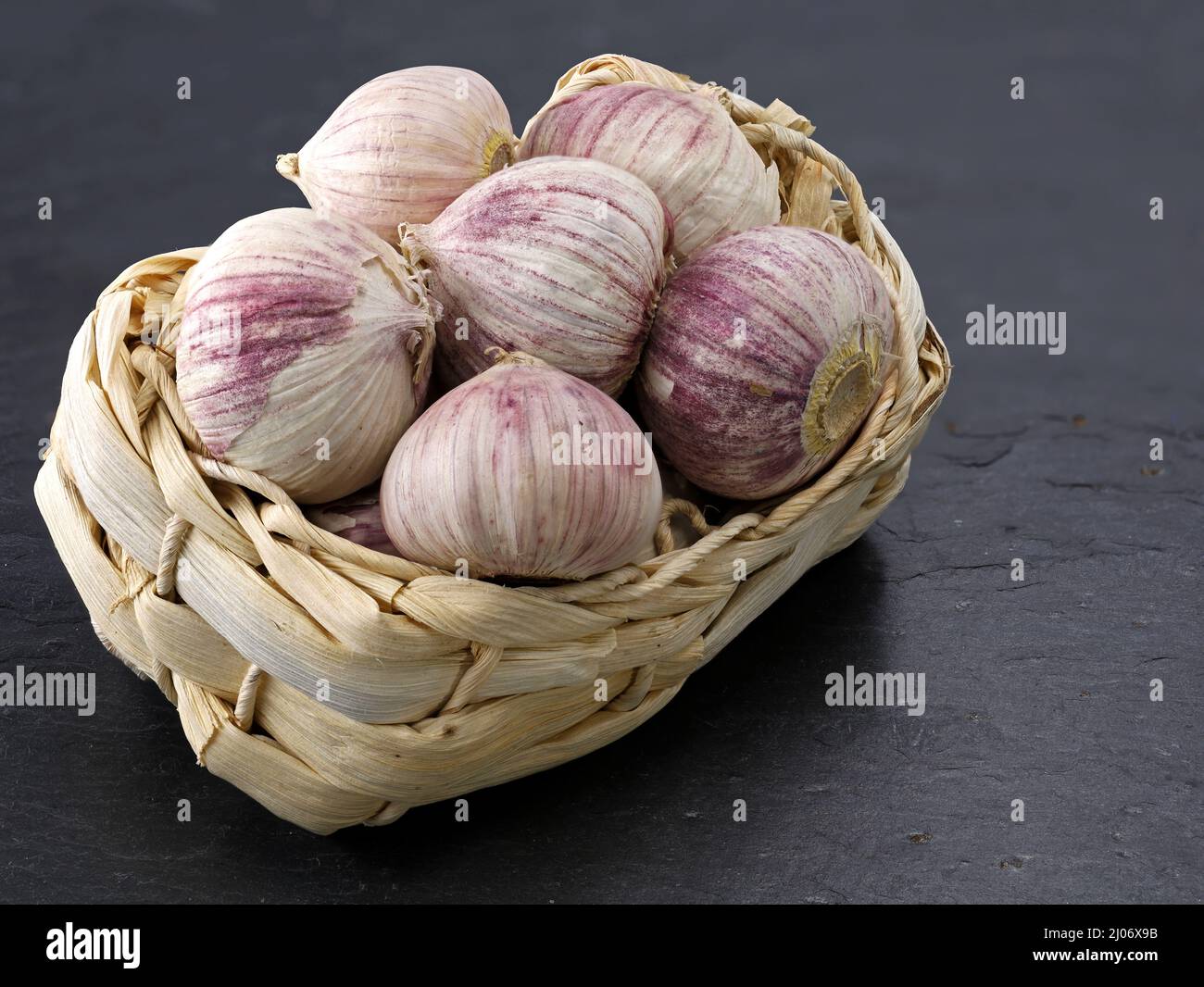 solo garlic, allium sativum in straw basket isolated on black slate ...