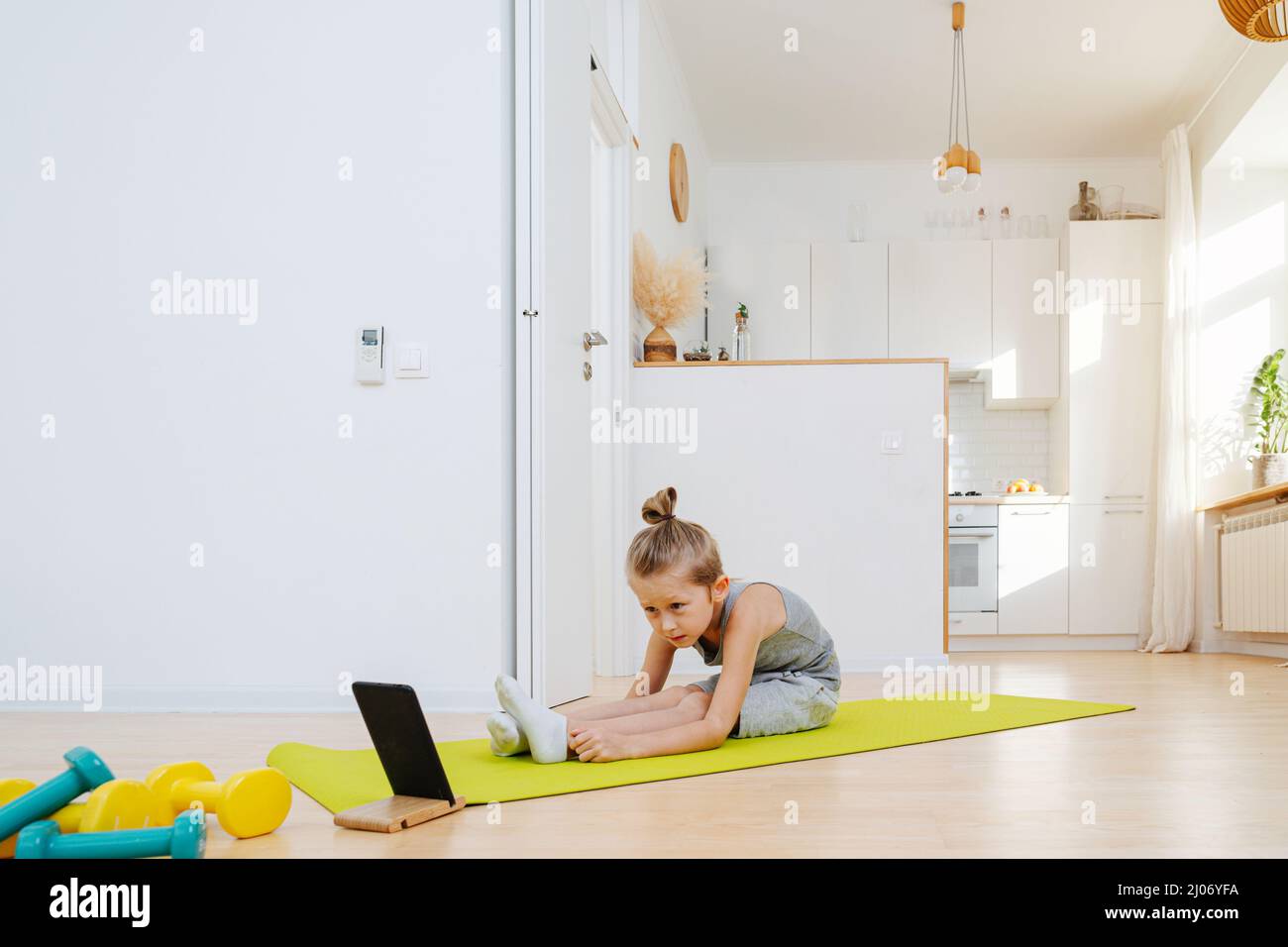 Cute boy doing yoga in front of a phone in a holder, following ...