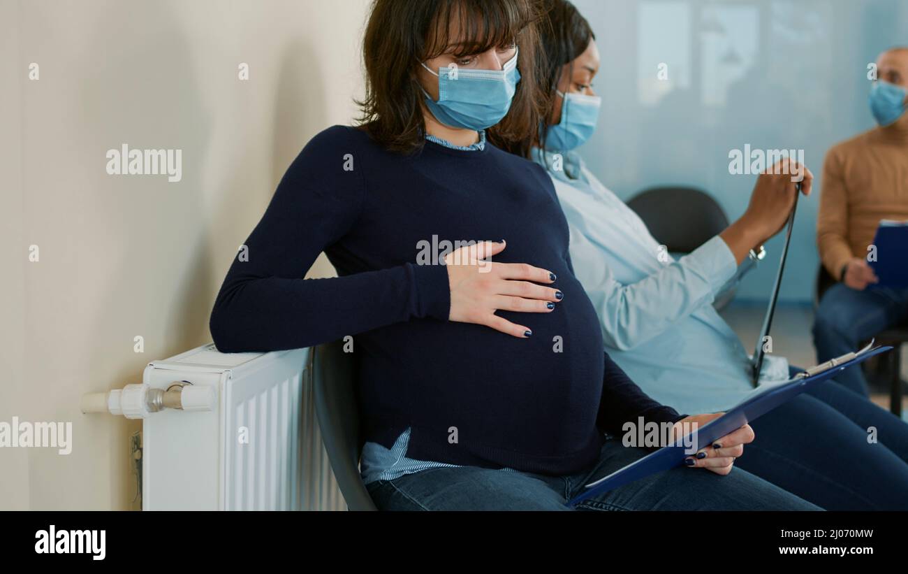 Pregnant woman with face mask sitting in waiting queue at job interview ...