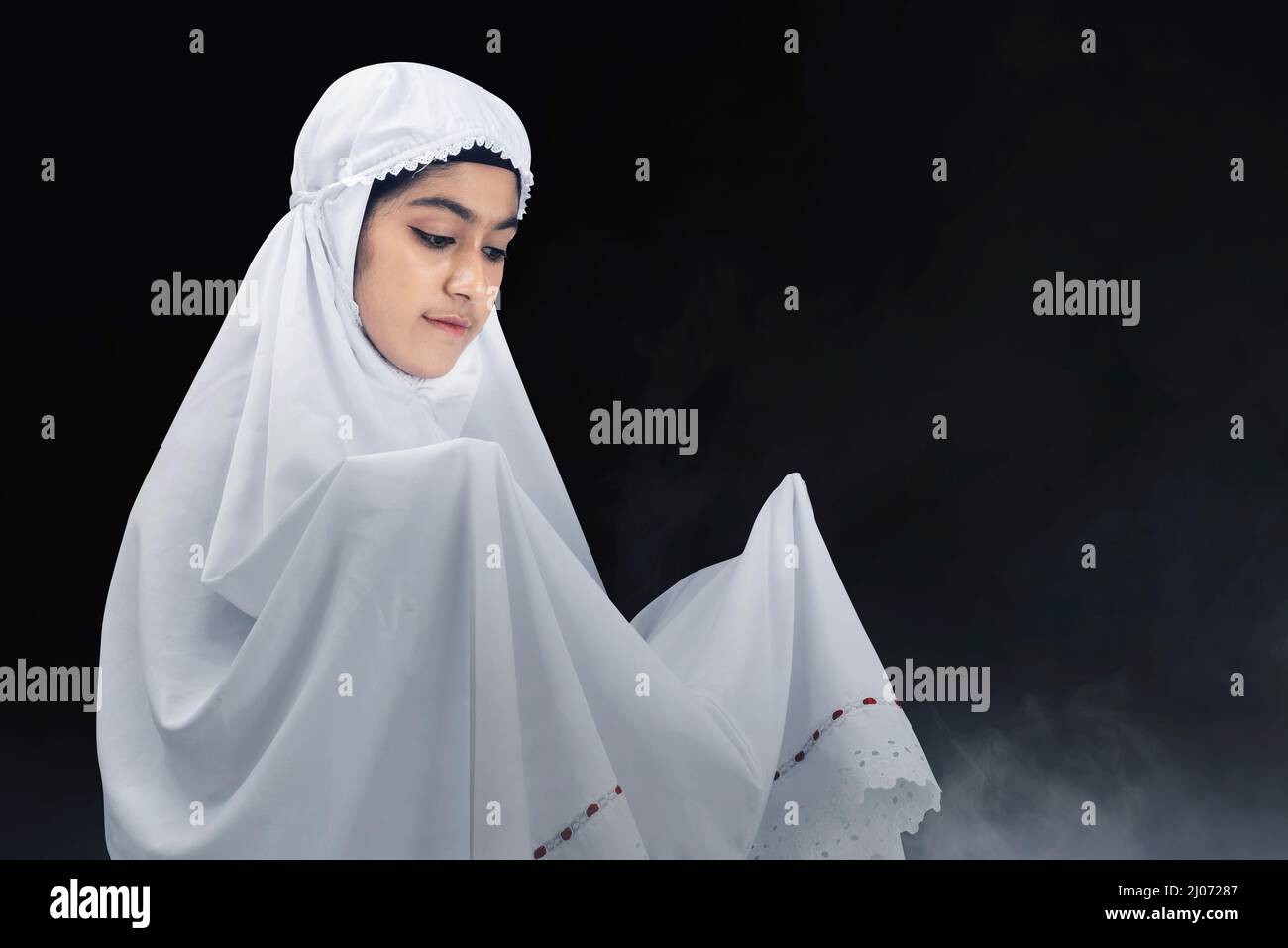 Asian Muslim woman in a veil standing while raised hands and praying ...