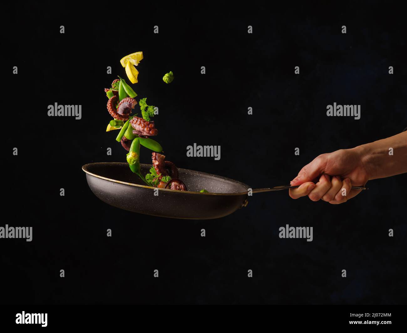 On a black background, a frying pan with seafood and vegetables in the ...
