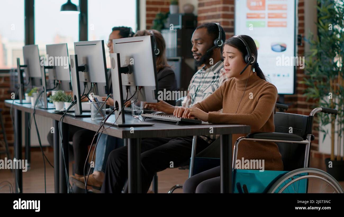 Asian woman with disability using headset to help clients at call ...