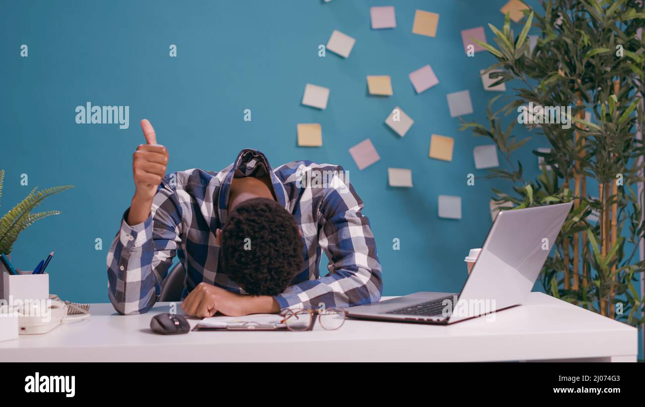 Overworked man putting head on desk and showing okay sign, giving ...