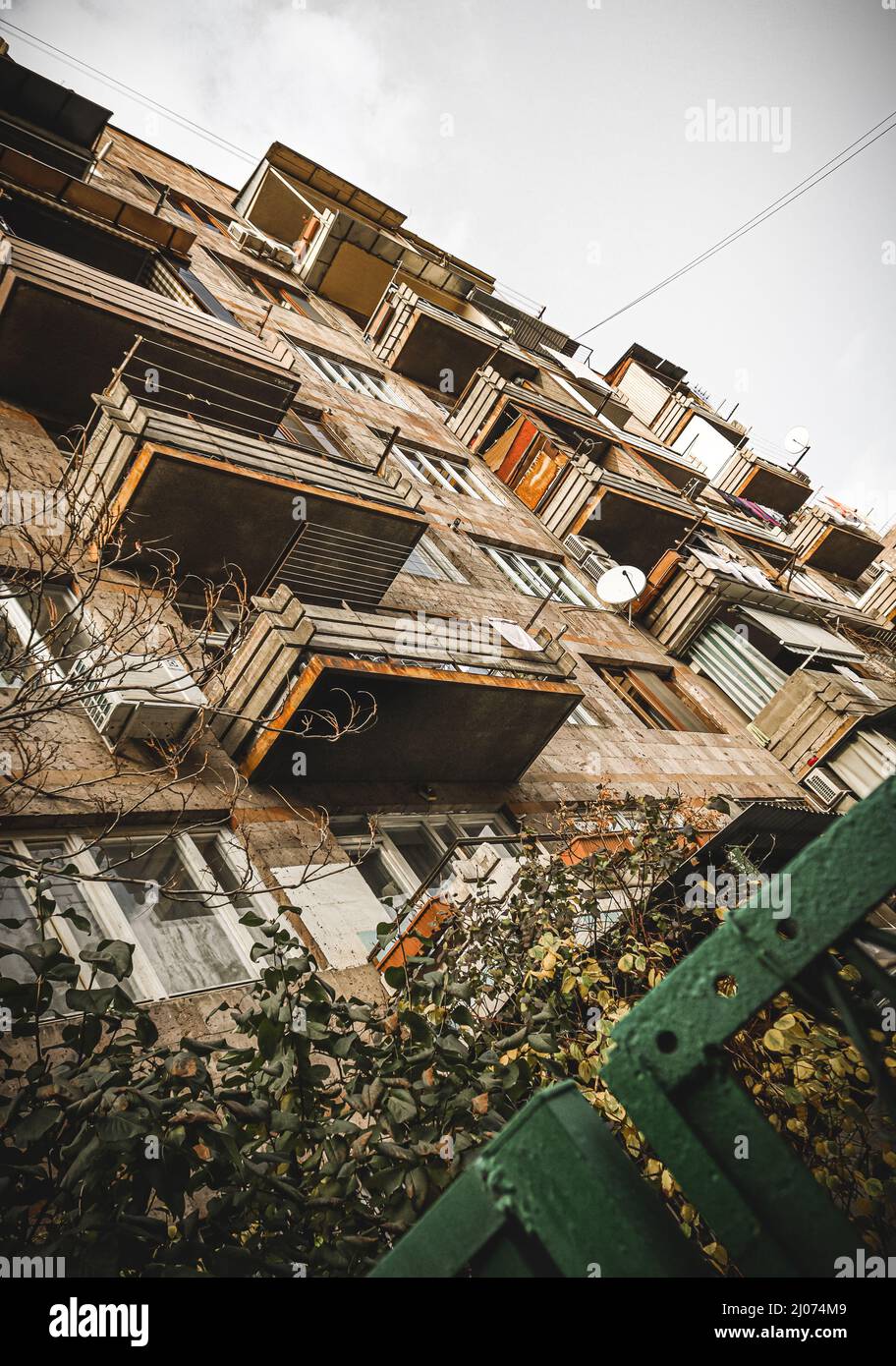 Vertical low angle shot of an old apartment building with balconies on a gray sky background ...